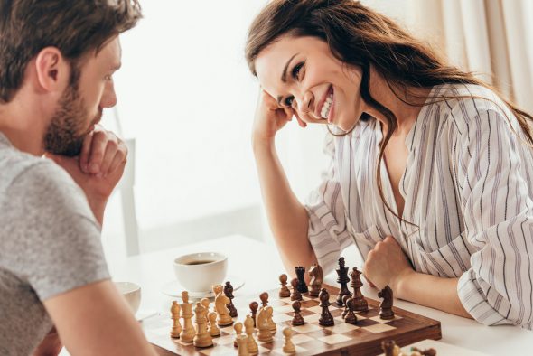 young couple playing chess while sitting at table at home - Unpacked